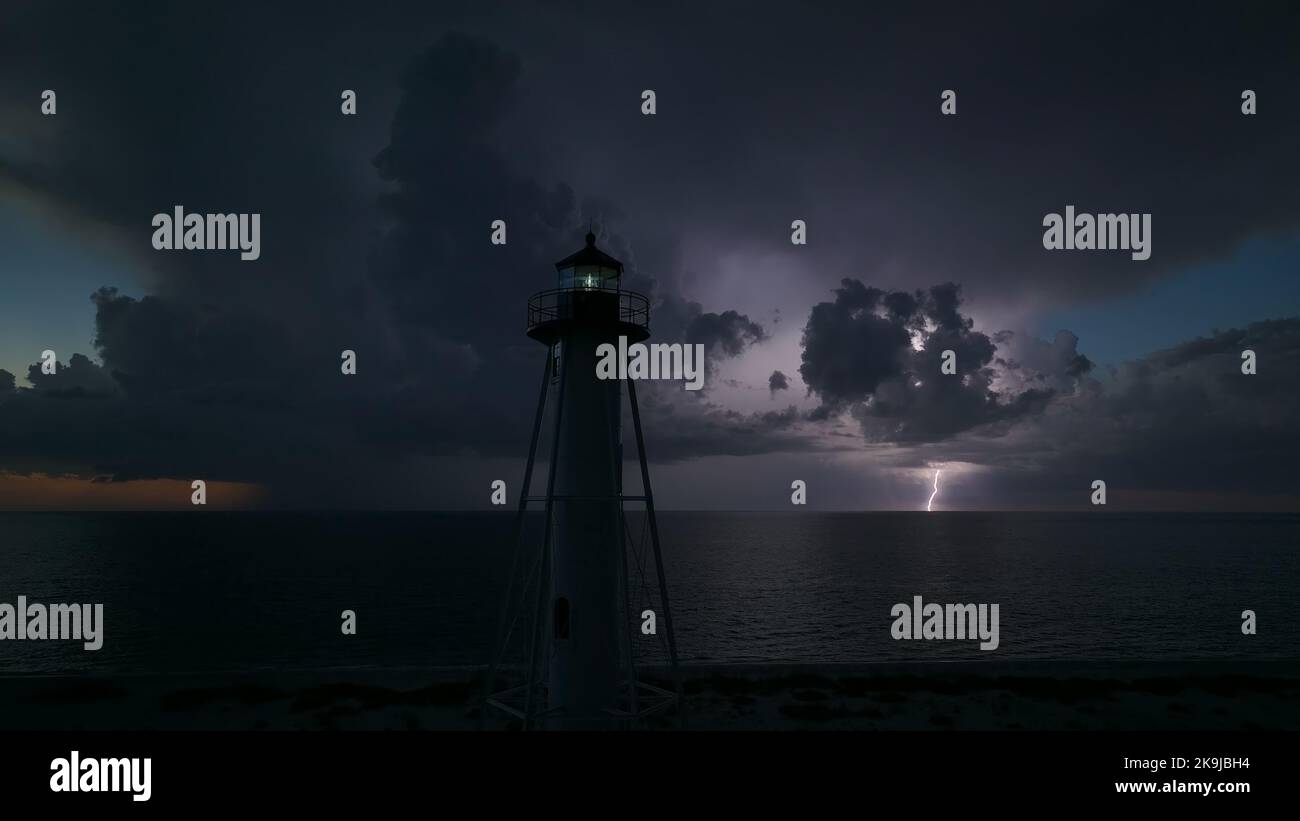 White tall lighthouse on sea shore with blinking light at stormy night ...