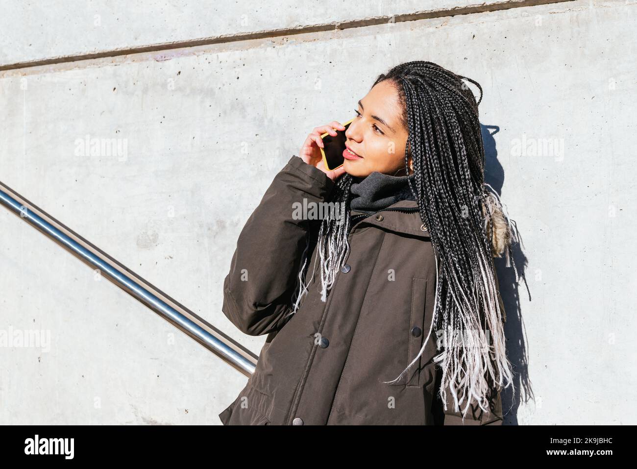 Serene female with braided hair having conversation on smartphone while ...