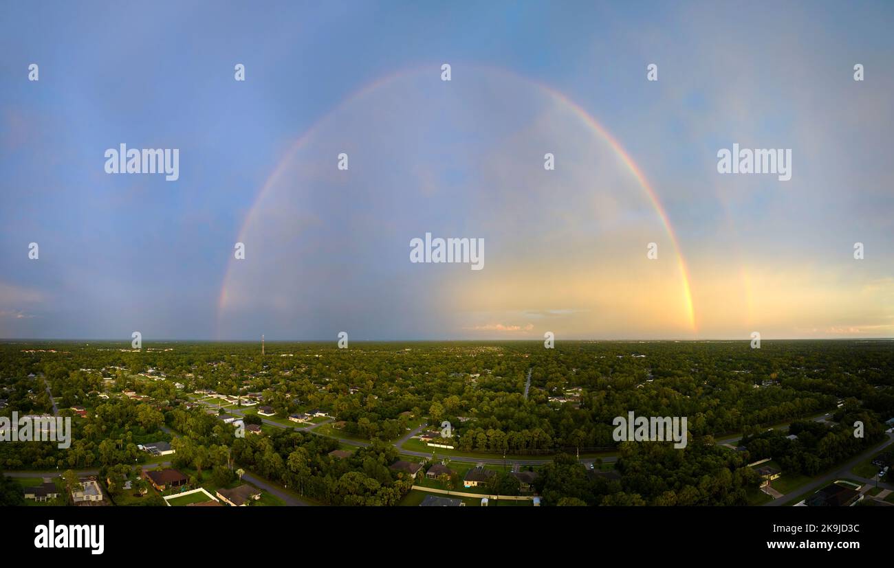 Colorful round rainbow over rural town suburbs against blue evening sky ...