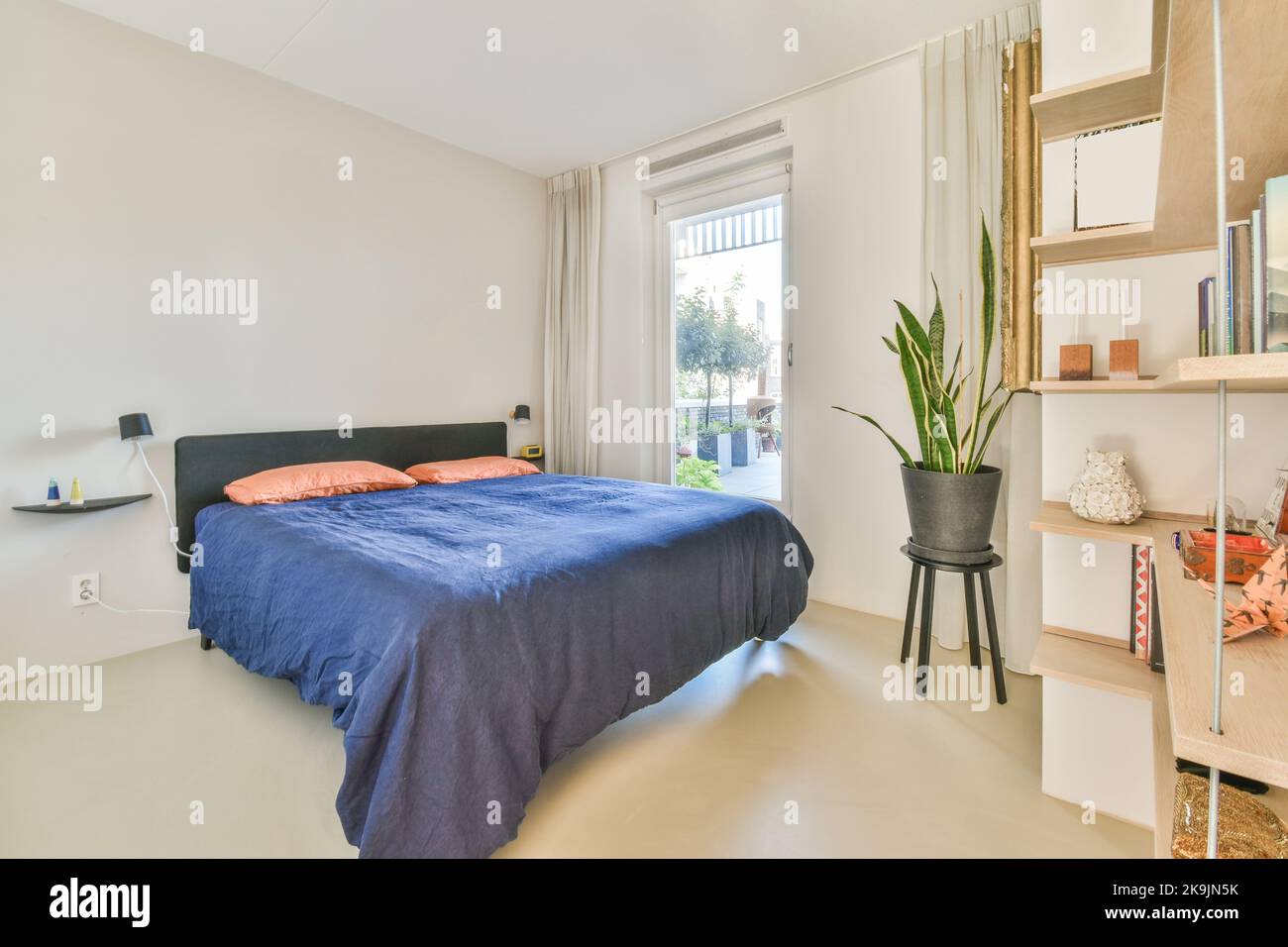 Comfortable bed located near balcony door with curtains in cozy light ...