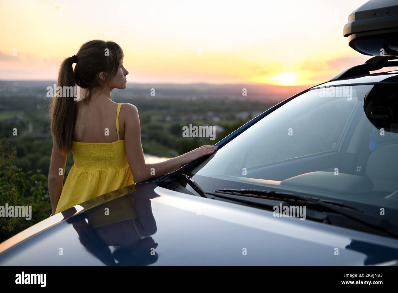 Happy young woman driver in yellow dress leaning on her car enjoying ...