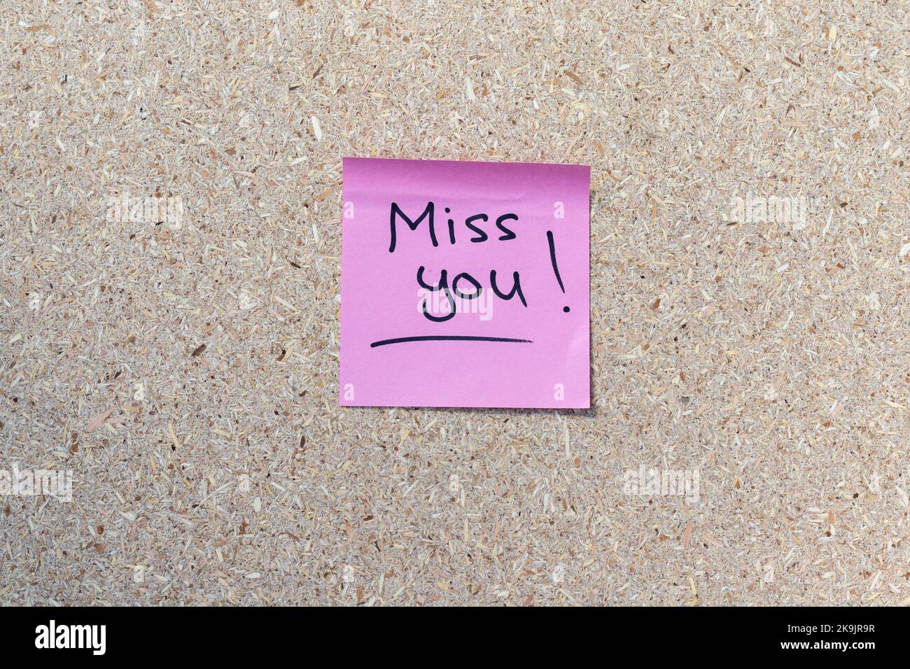 A hand written reminder note of a text Miss You on a pink sticky note ...