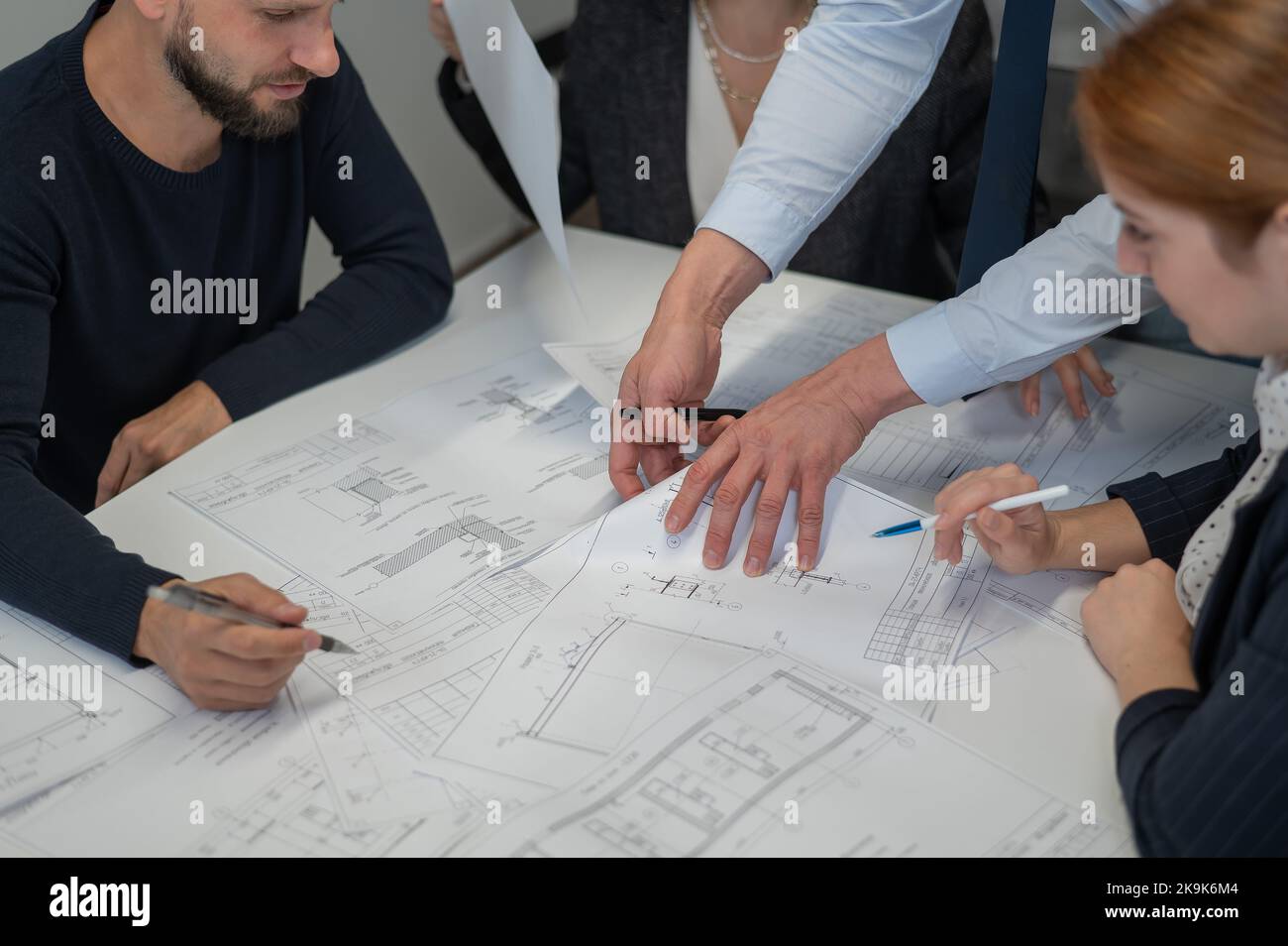 Close-up of the hands of four colleagues with blueprints on the table ...