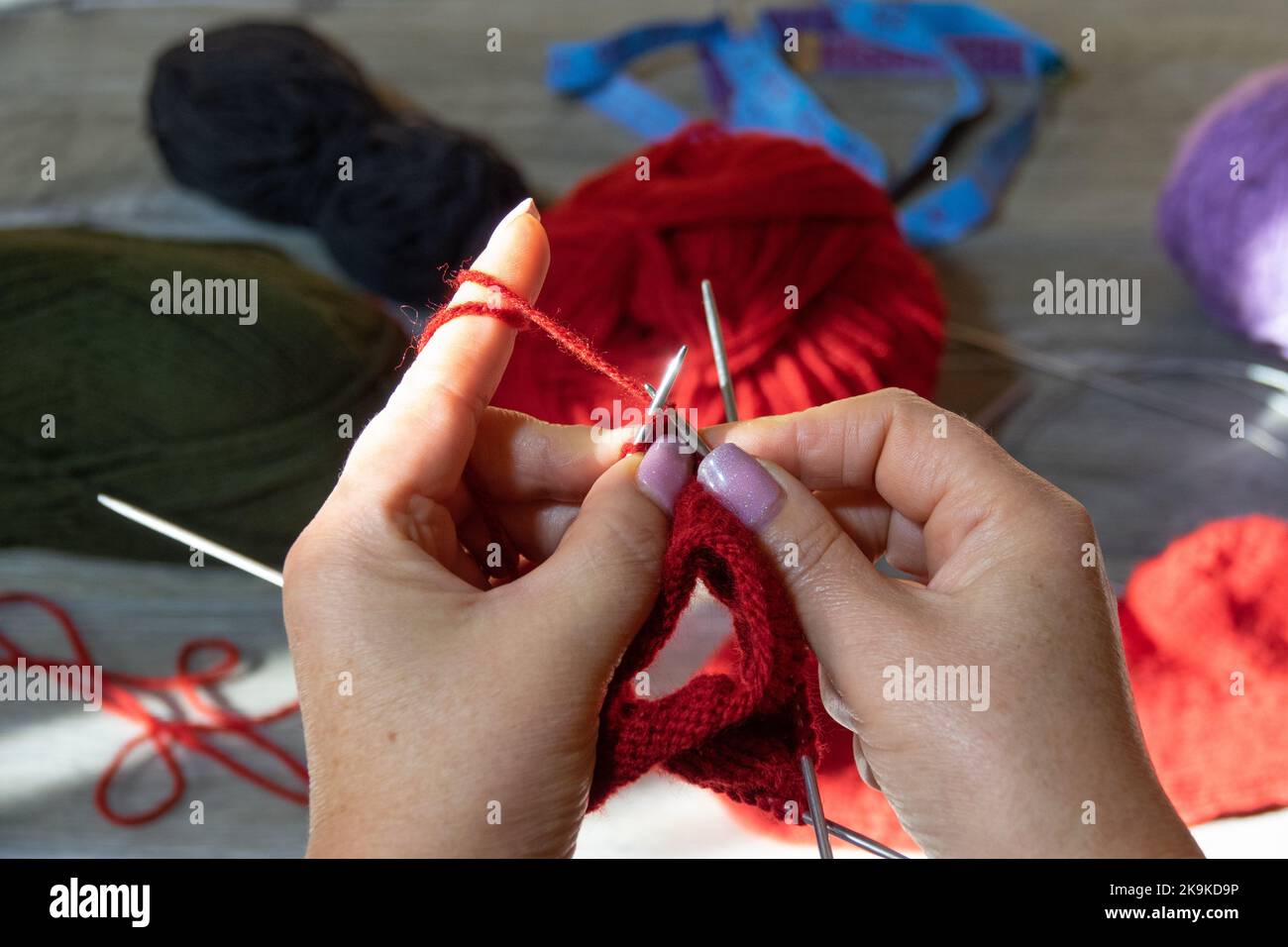 Woman hands knitting sock with needles and yarn of red color. Clews ...