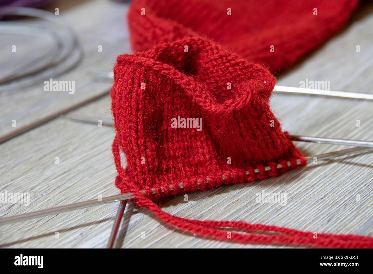 Sock in the process of knitting with needles and yarn of red color on a ...