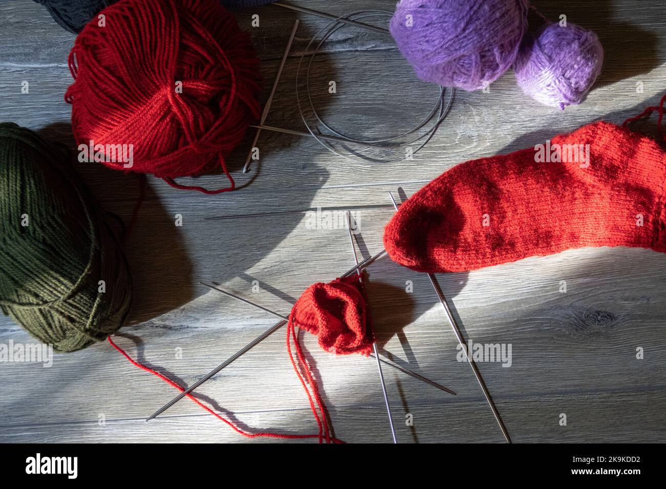 Sock in the process of knitting with needles and yarn of red color on a ...