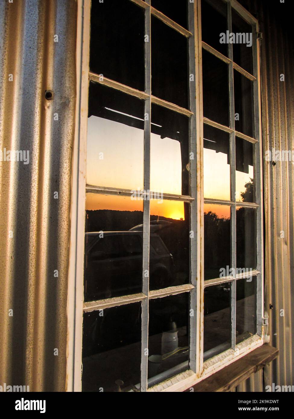 Sunset reflecting in a window in an old house built of corrugated iron ...