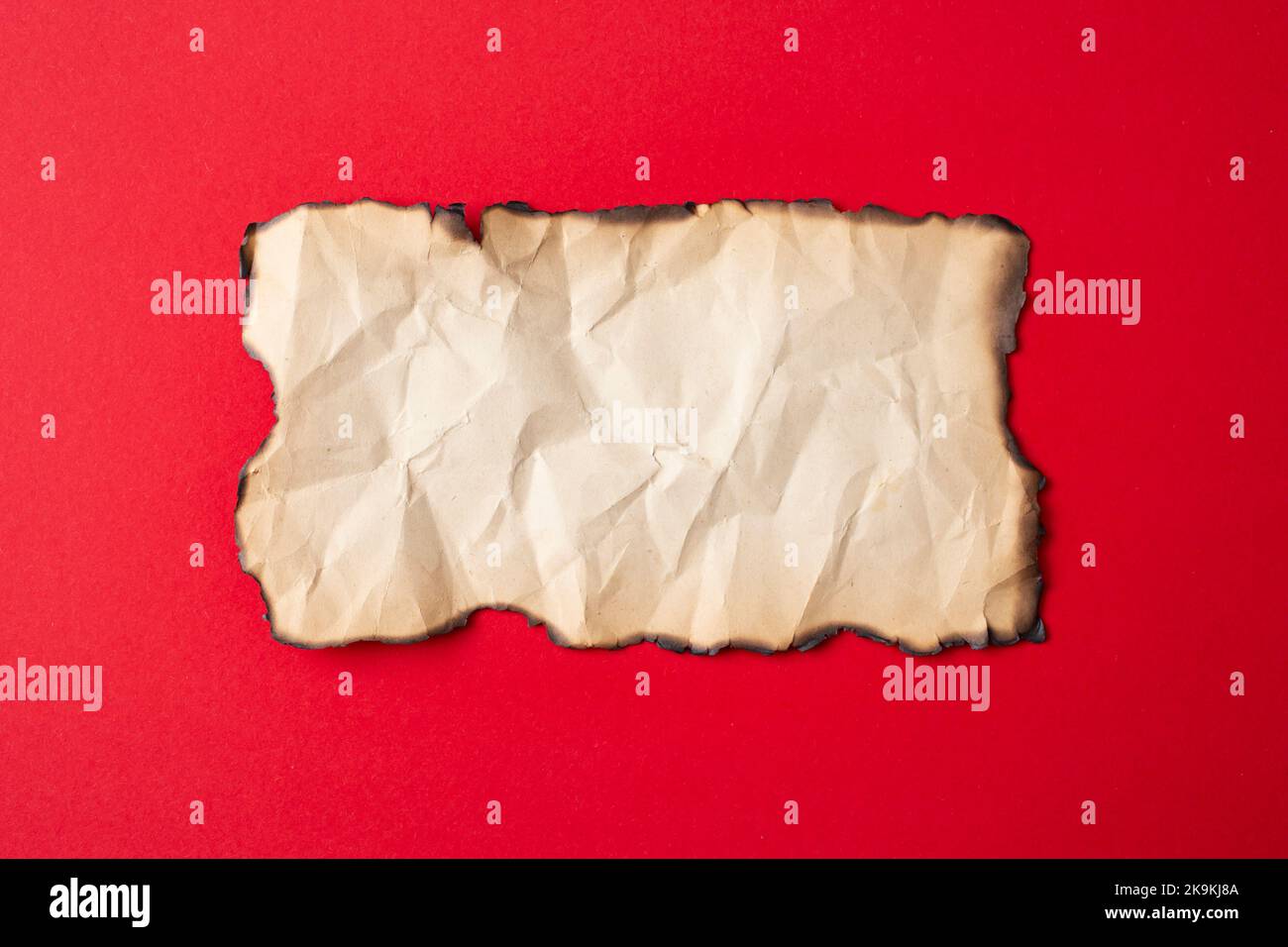 Vintage crumpled paper with burned edges, close up isolated on red ...