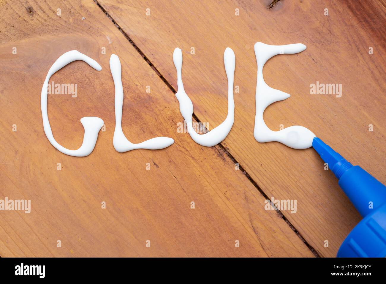 glue written on wood texture with white clay glue, dripping from a blue ...