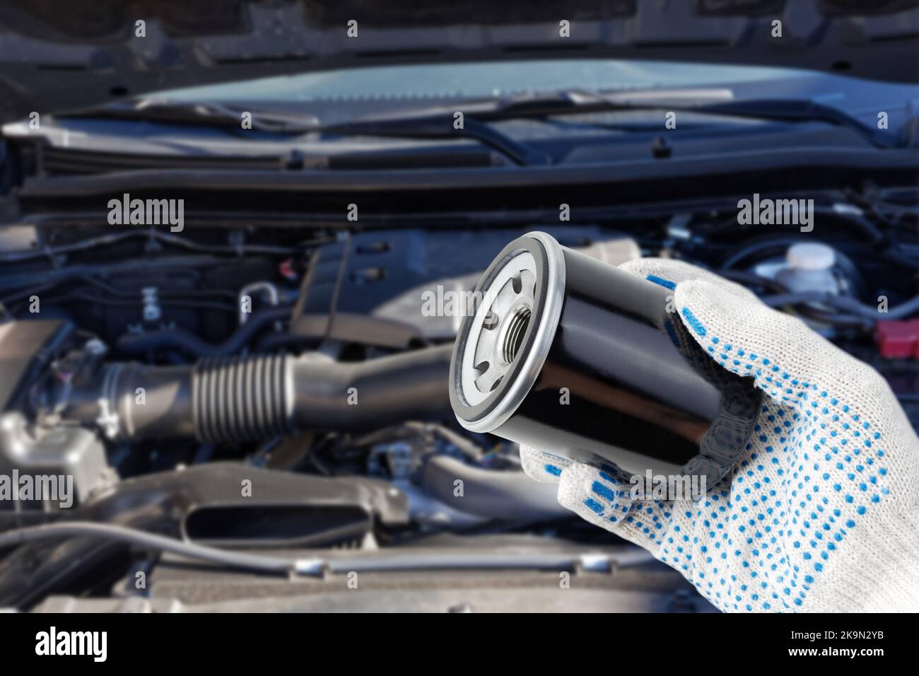 Auto mechanic holds an oil filter in his hand for replacement and car ...
