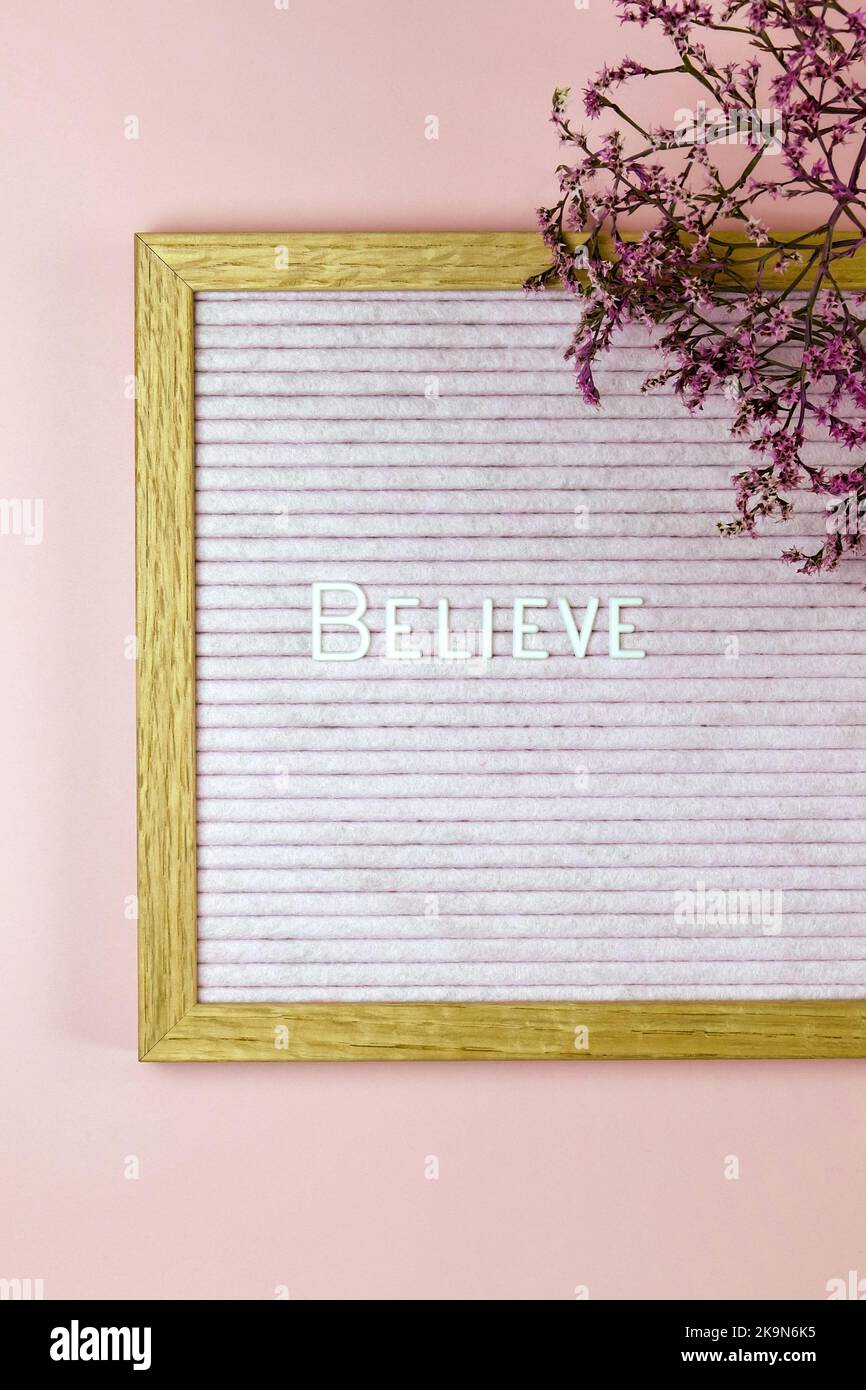 Word BELIEVE from white letters on letter board and and branch of pink ...