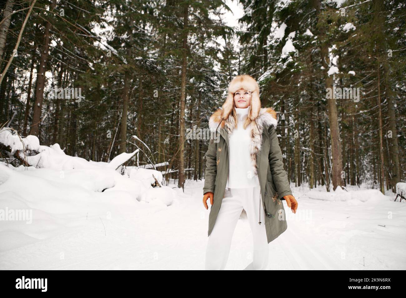 Young woman stand in winter forest, look up at fir trees and snow ...