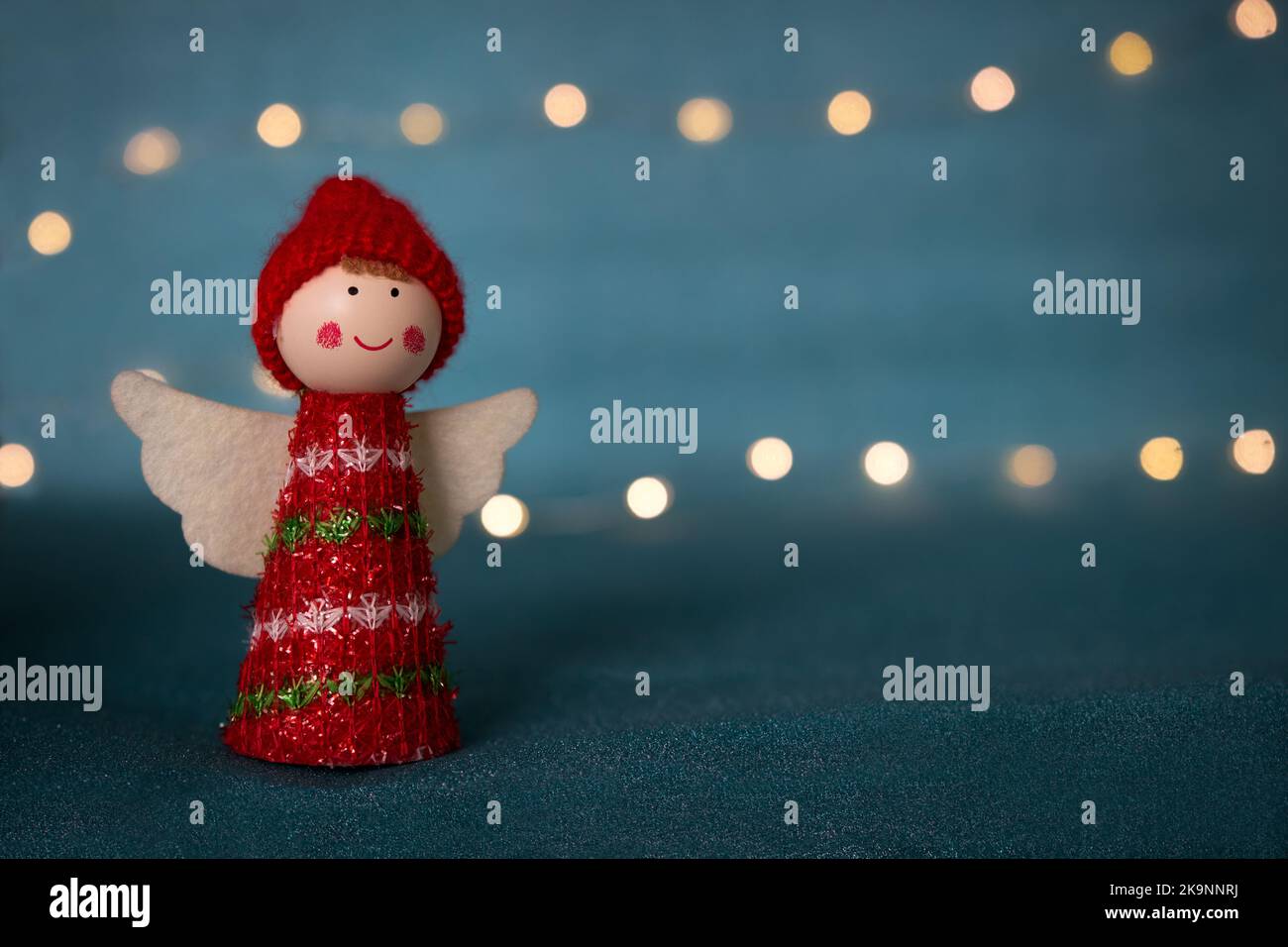 A cute red Christmas angel statuette with bokeh fairy lights on a ...