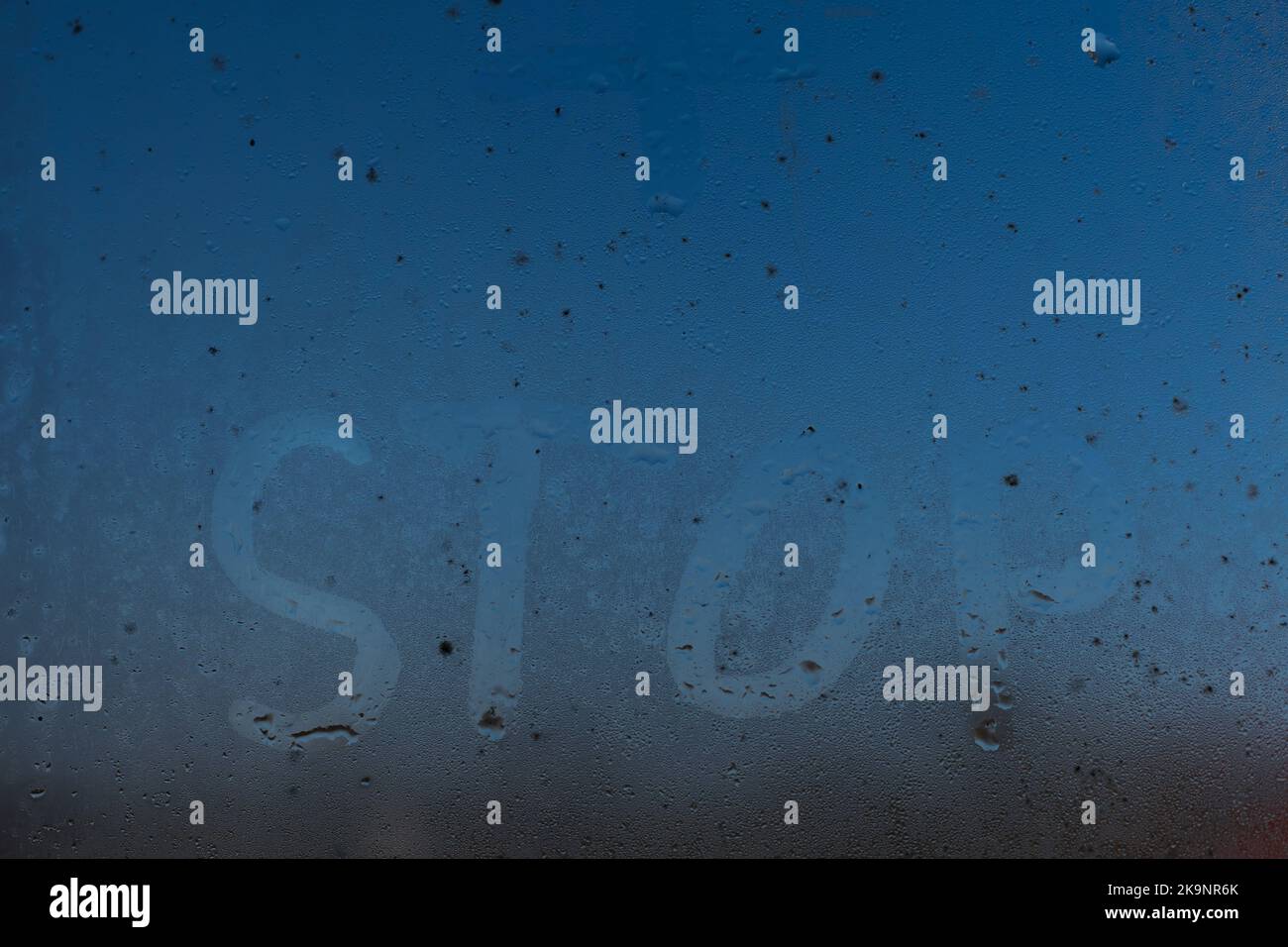 the word stop written on night wet window glass close-up with blurred ...