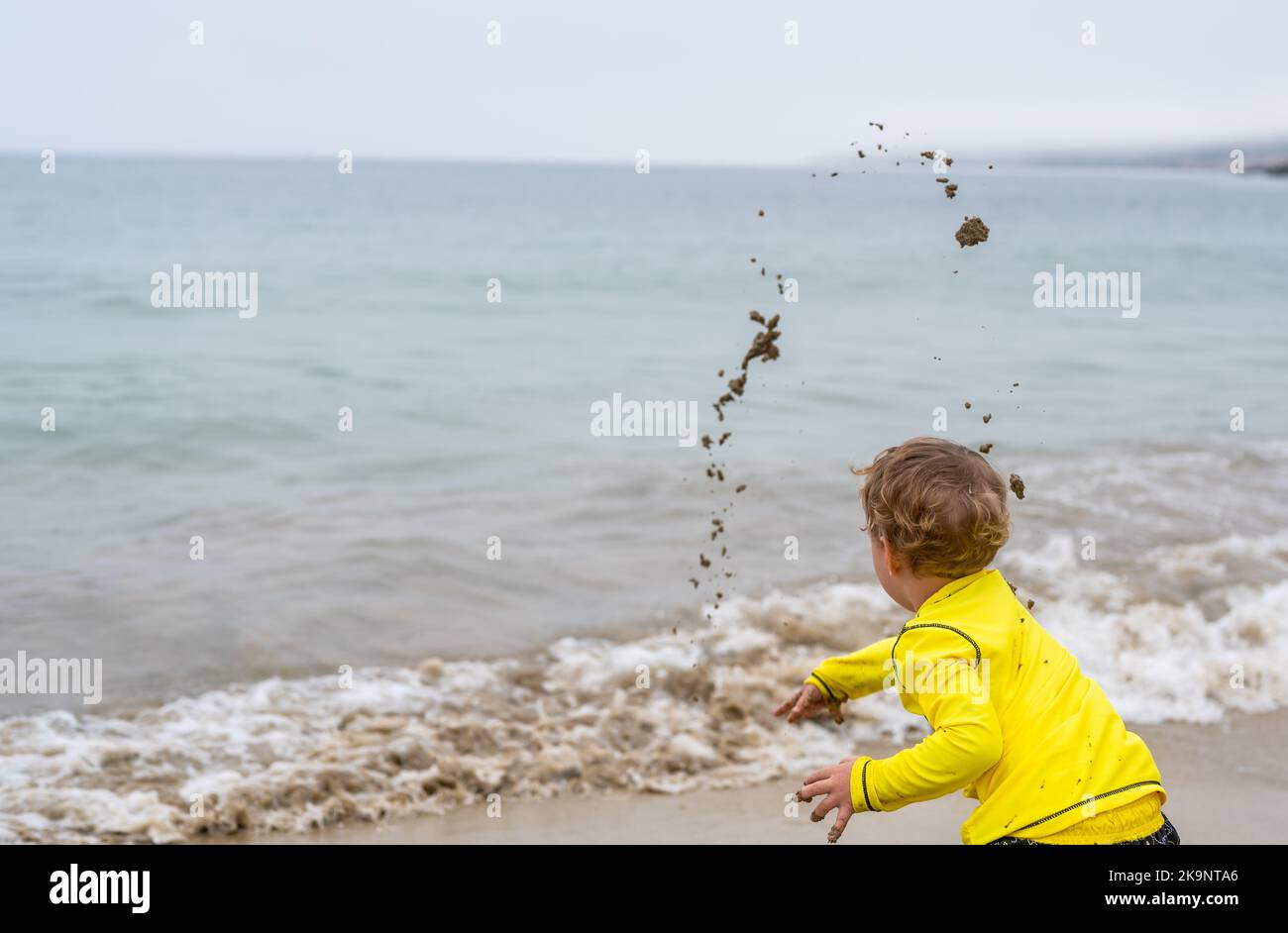 Young child in a swimsuit throwing sand into open water Stock Photo - Alamy