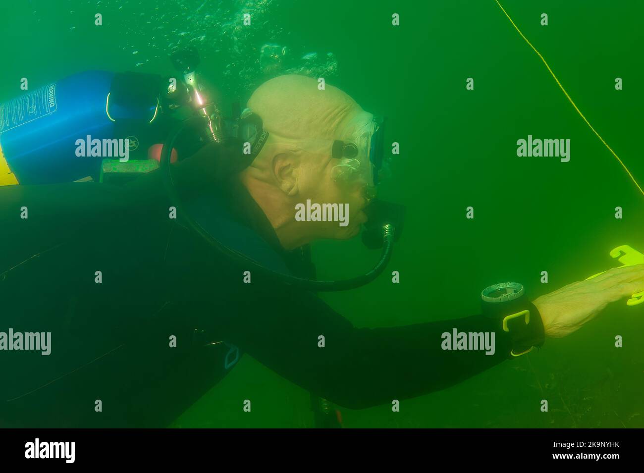 A bald SCUBA diver exploring a murky inland lake with dive flag line in ...