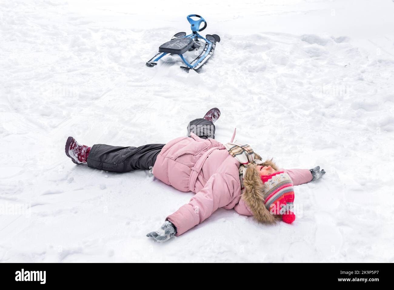 A little girl lies in the snow in the winter in the park. Happy ...