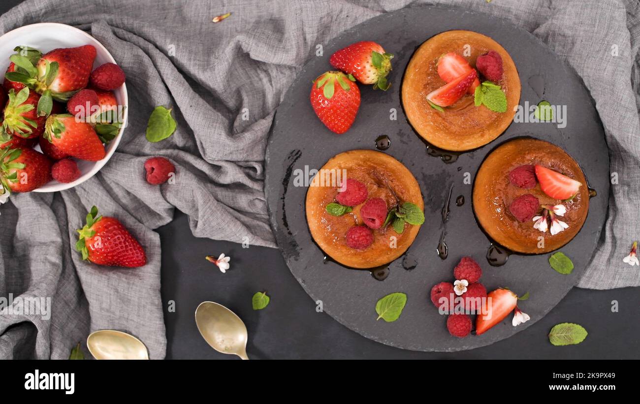 Caramel custard puddings on round slate on and dark kitchen countertop ...
