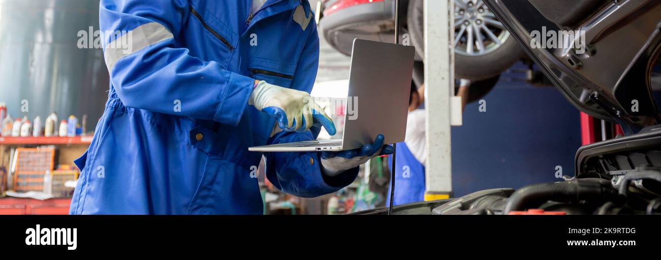 Young man is mechanic using laptop computer checking engine of car in ...
