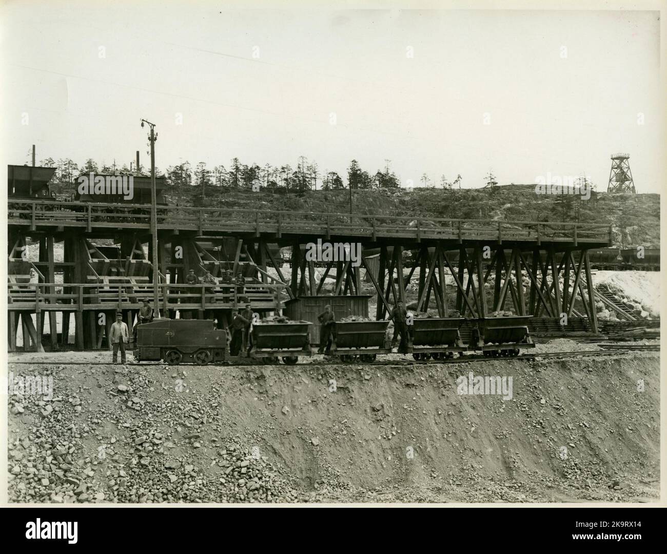 A motor locomotive with ore trolleys stands below the ore loading ...
