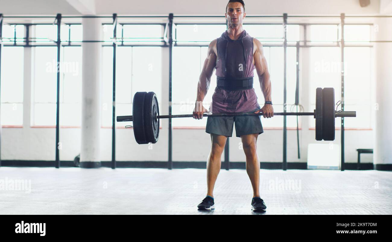 The incredible bulk. a muscular young man lifting a barbell in a gym ...