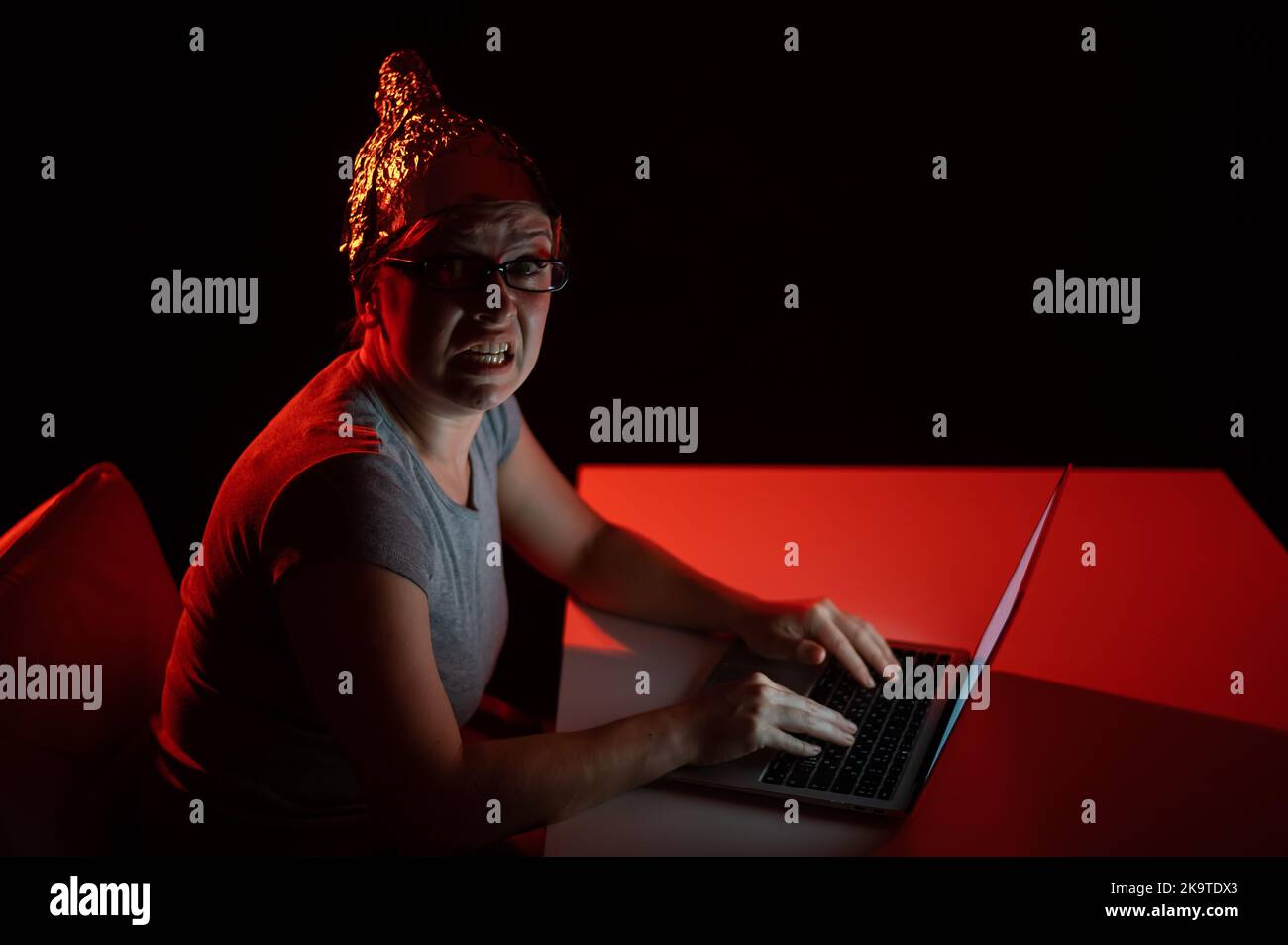 Paranoid caucasian woman typing on a computer wearing a tinfoil cap ...
