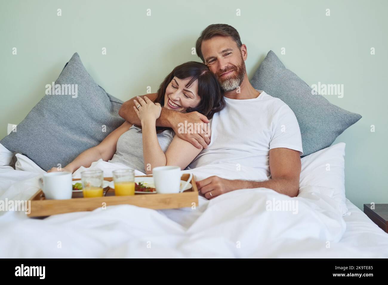 Leave me alone while I eat. a cheerful young couple sitting in bed ...