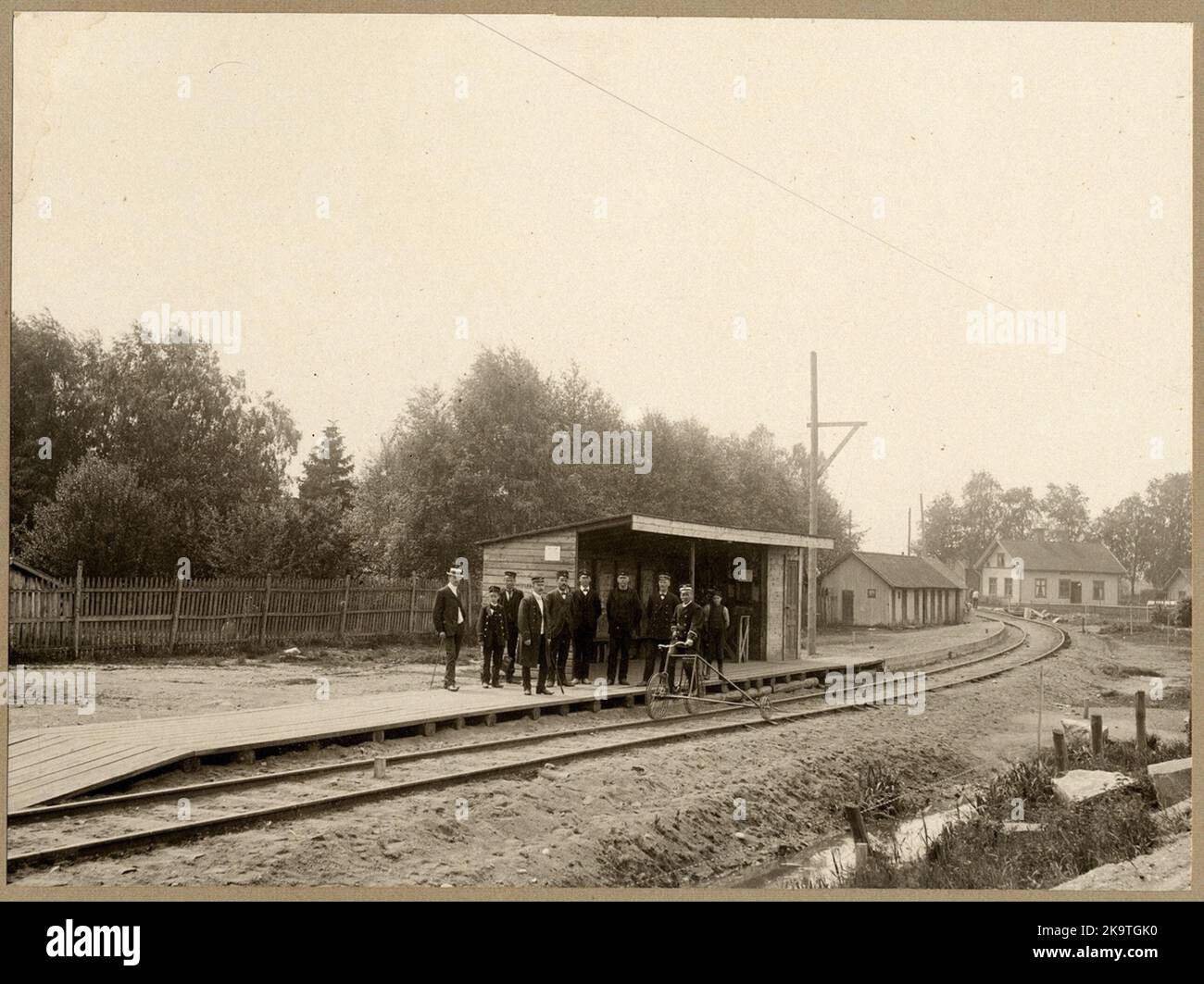 Tidaholm 1907. 10 people in front of a shed. Man on three -wheeled ...