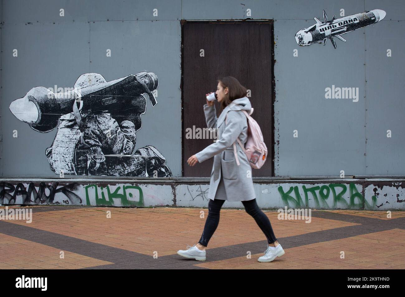 A girl passes by graffiti depicting a Ukrainian serviceman making a ...