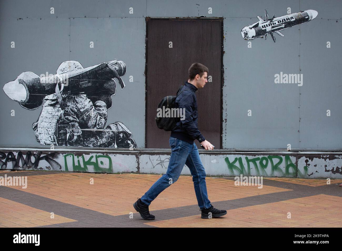 A man passes by a graffiti depicting a Ukrainian serviceman making a ...