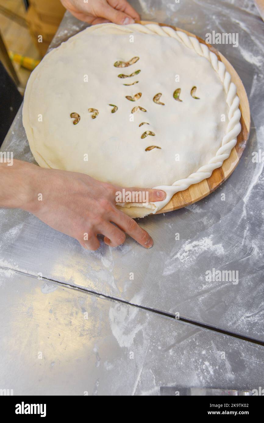 Hands closing the Ossetian pie stuffed with minced meat on the metal ...