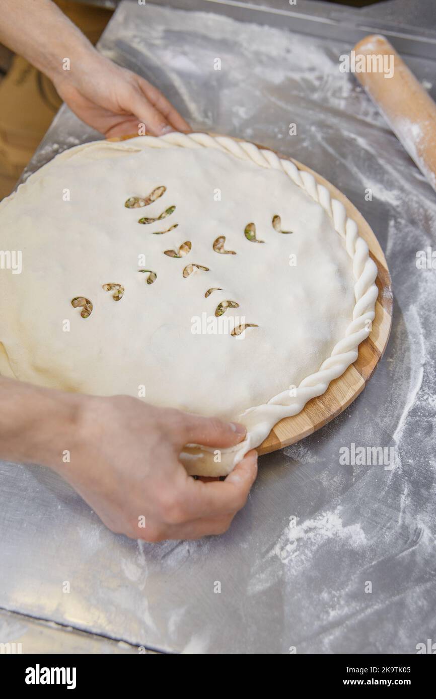Hands closing the Ossetian pie stuffed with minced meat on the metal ...