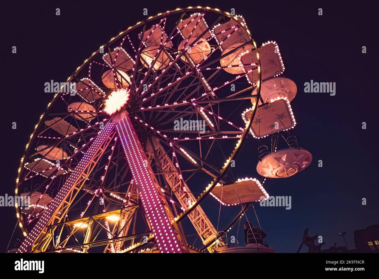 Funfair ferris wheel at night. Ferris wheel and rollercoaster in motion at amusement park at ...