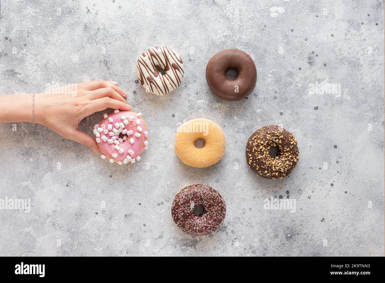Female hand holding fresh donuts, assortment of various colourful ...