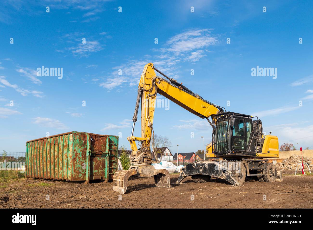 An excavator stands next to a rubble container Stock Photo - Alamy
