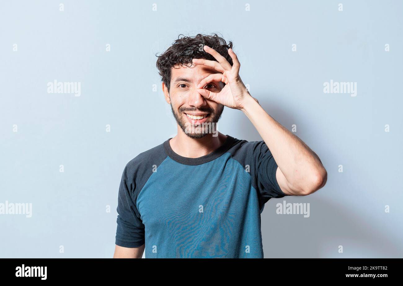 Friendly guy making ok gesture looking through fingers. Happy young man ...