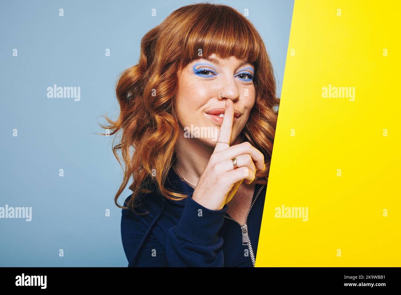 Woman making a hush gesture while standing next to a geometric shape ...