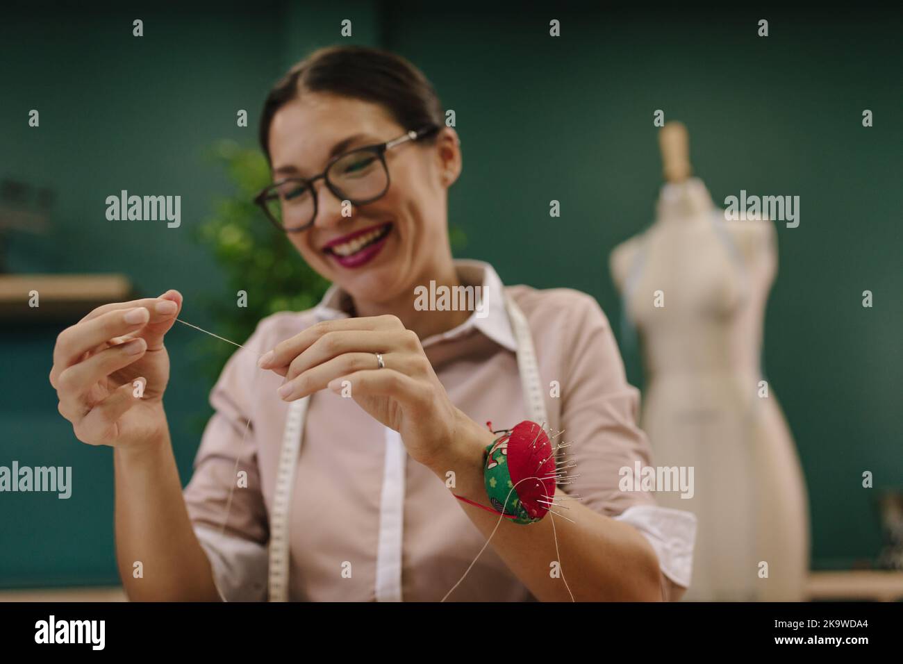 Woman dressmaker smiling and threading the needle at fashion studio ...