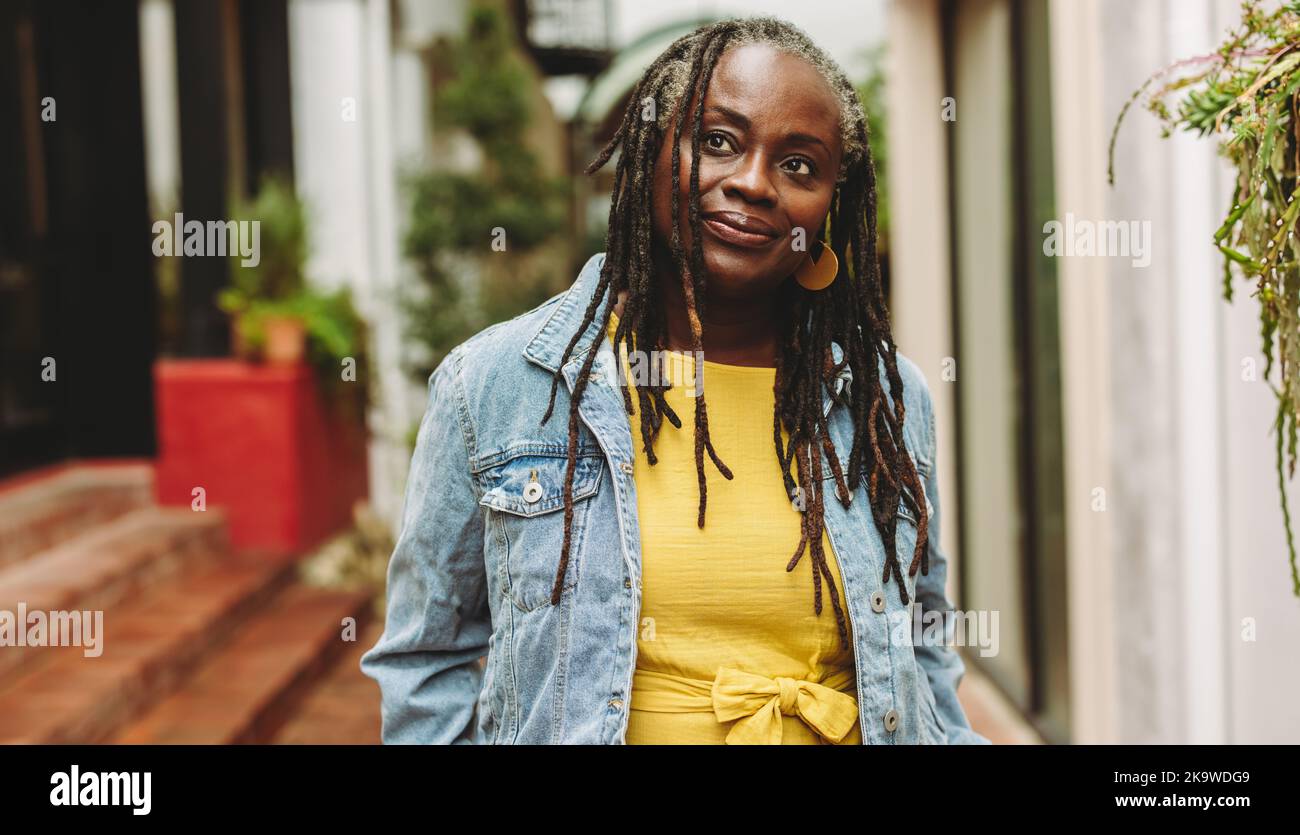 Mature woman with dreadlocks looking away thoughtfully while standing ...