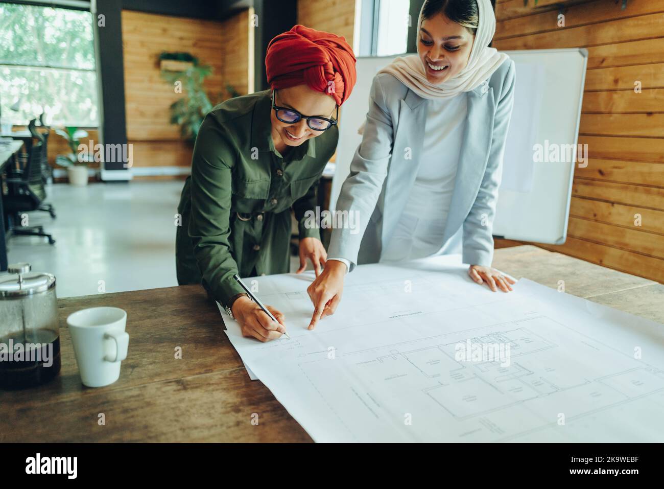 Cheerful Muslim architects working on blueprint drawings in a modern office. Two creative ...