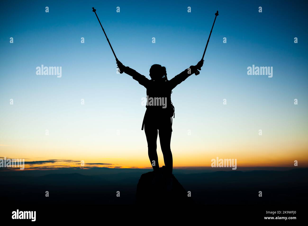 Silhouette of a hiker girl on a rock pedestal with hands up. Beautiful ...