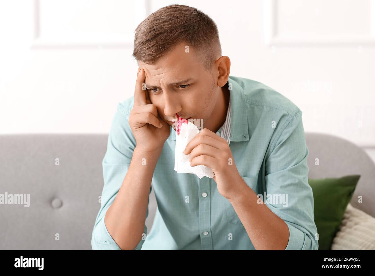 Young man with nosebleed and tissue at home Stock Photo - Alamy