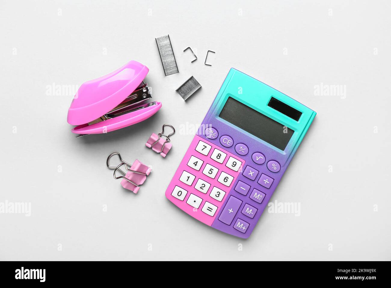 Pink stapler, calculator, staples and paper clips on light background ...