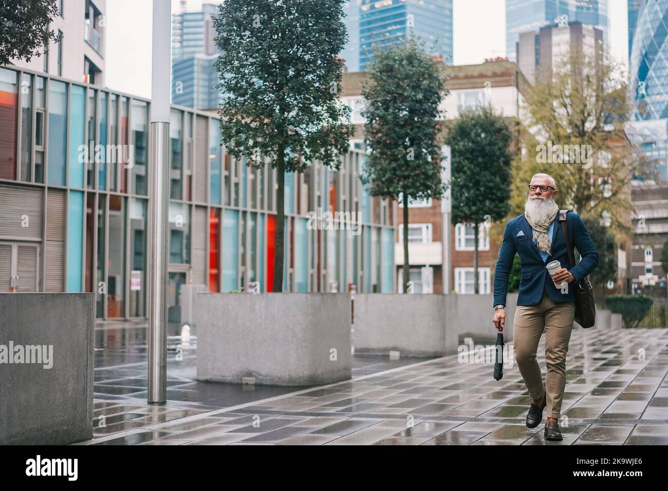 Happy business senior man walking to work on autumn rainy day - Focus ...
