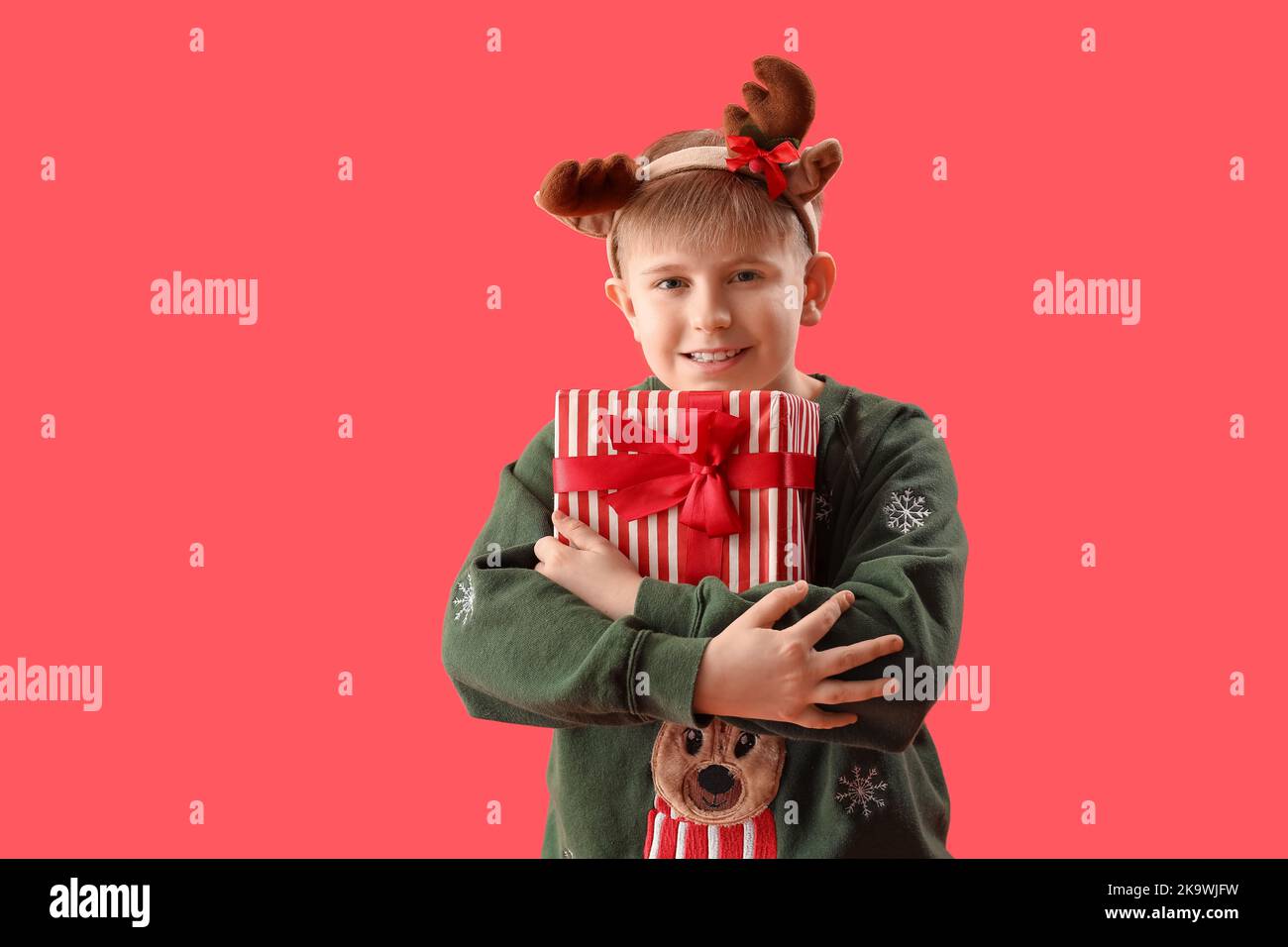 Happy little boy in reindeer horns with Christmas present on red ...