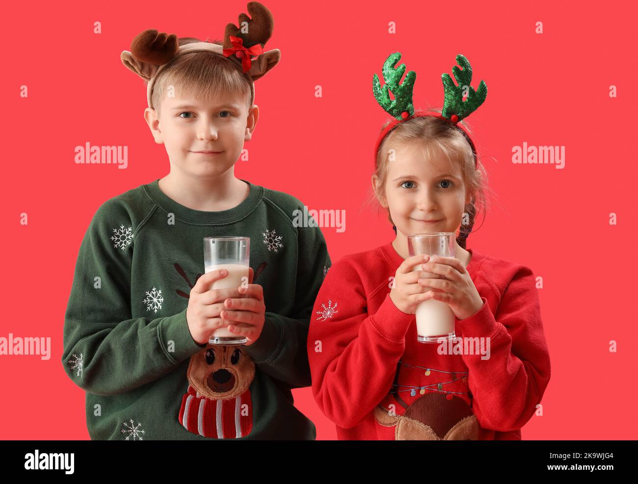 Happy little children in reindeer horns with glasses of milk on red ...
