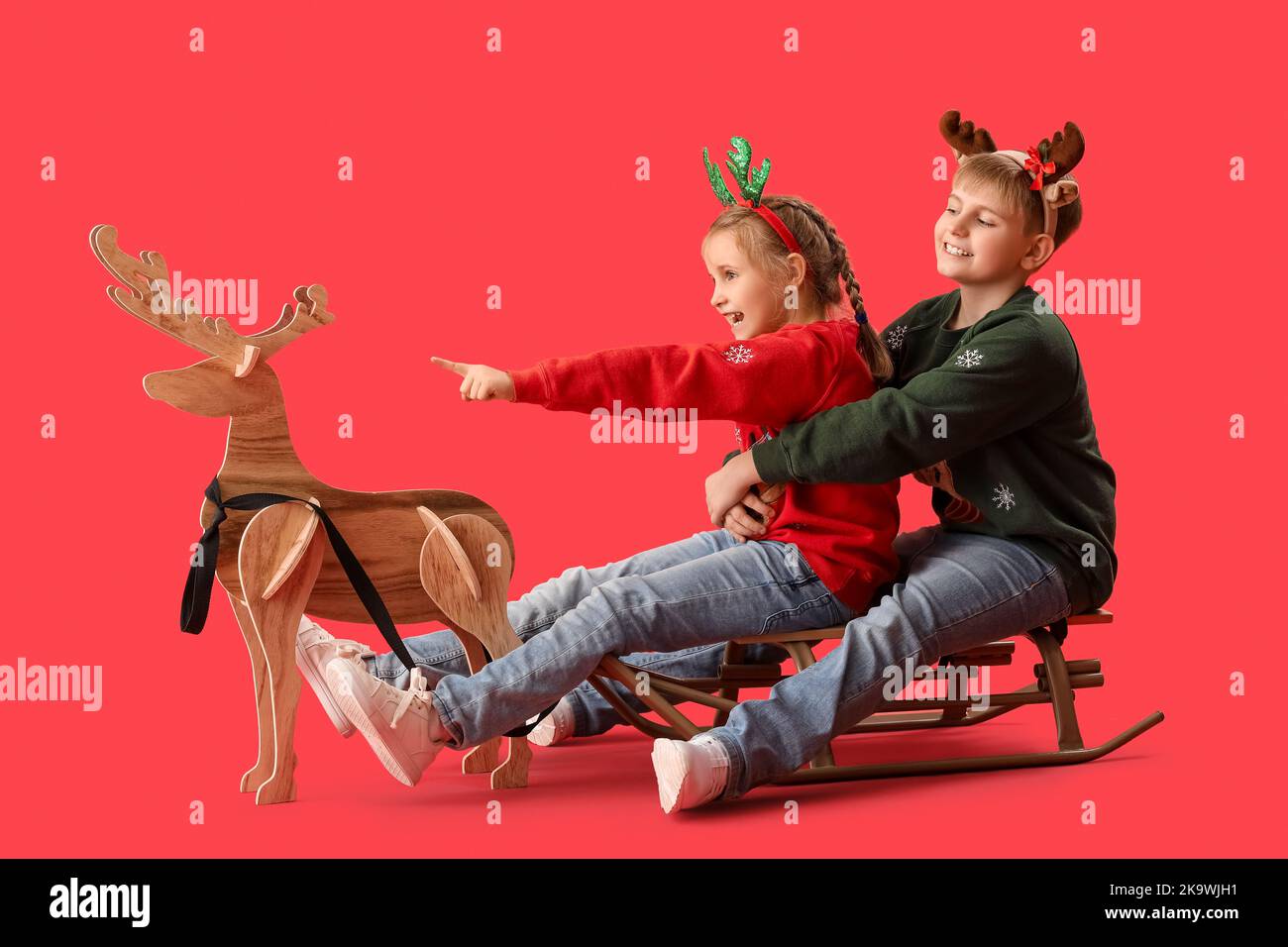 Happy little children with sledge and wooden reindeer on red background ...