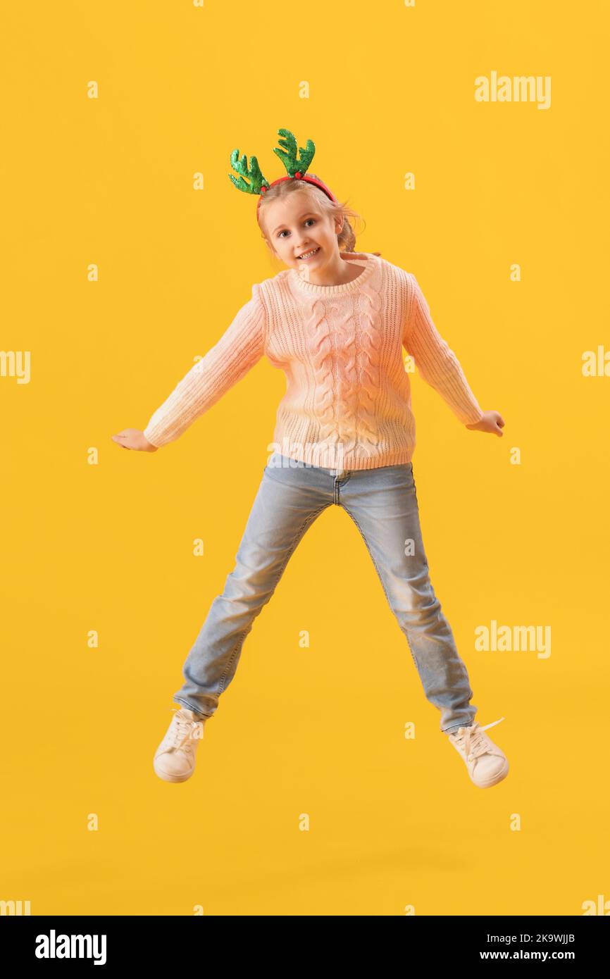 Happy little girl in reindeer horns jumping on yellow background Stock ...