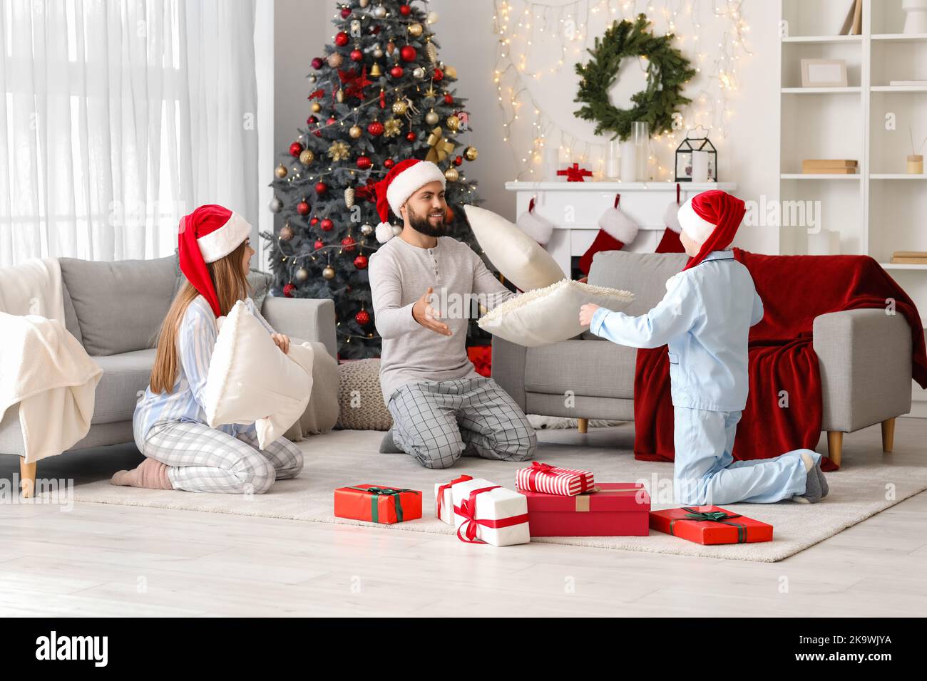 Happy parents with their little son in Santa hats fighting pillows at ...
