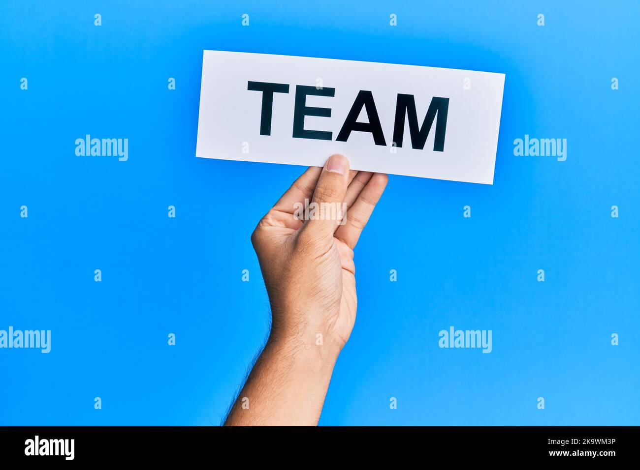 Hand of caucasian man holding paper with team word over isolated blue ...